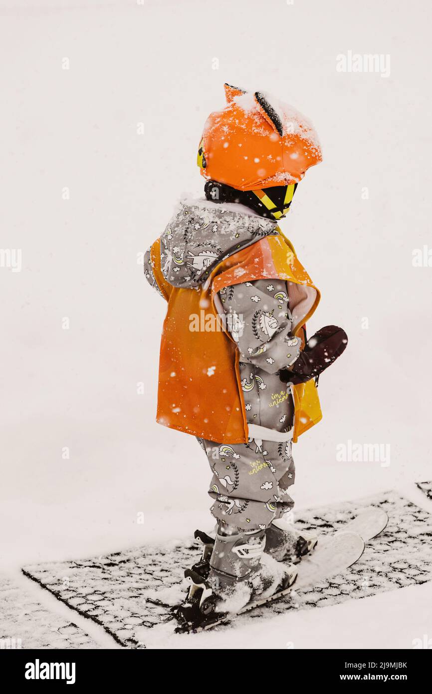 Back view of anonymous little kid in warm clothes and protective helmet ...