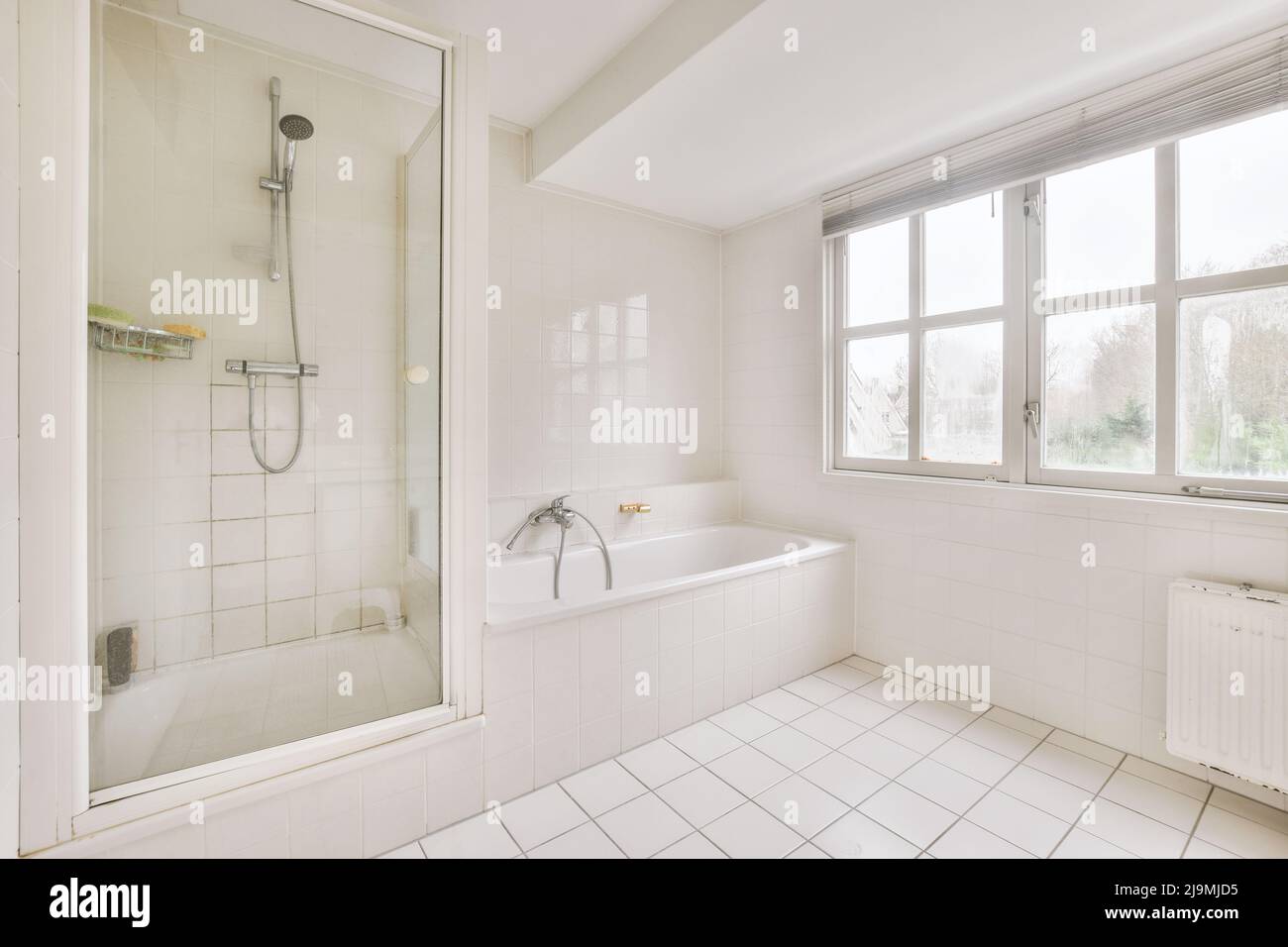 White ceramic tub placed near shower at tiled wall in light spacious ...