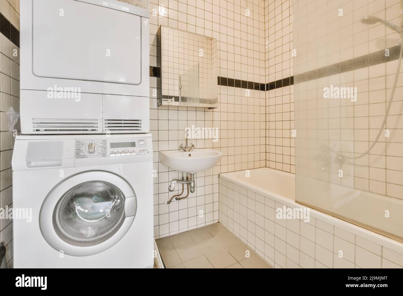 Interior of modern white tiled bathroom with washing machine and dryer ...