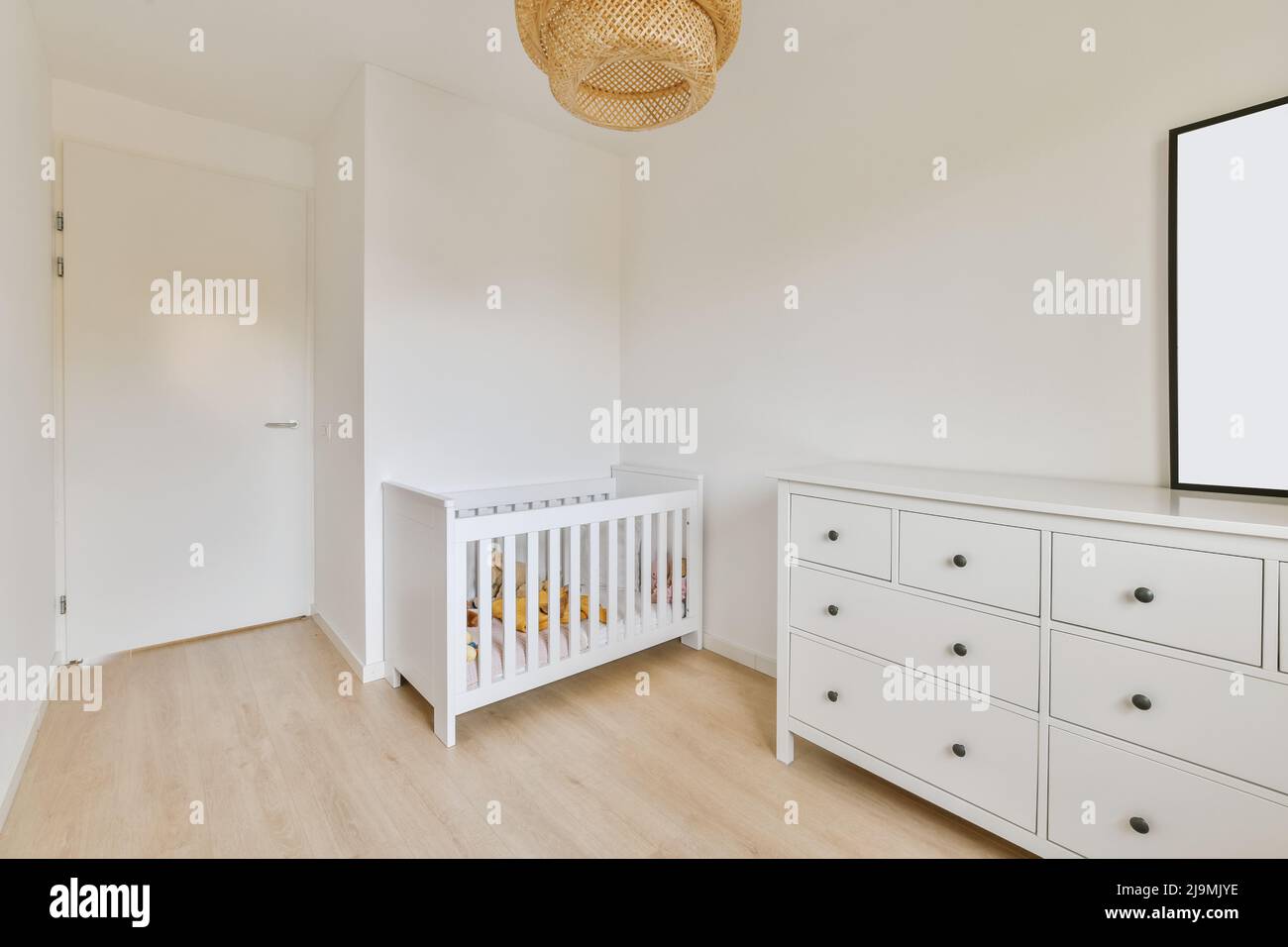 White crib and cabinet with empty frame located in sunlit minimalist ...