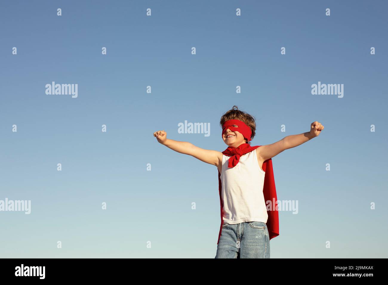 Low angle of adorable delighted little child with clenched fists in red ...