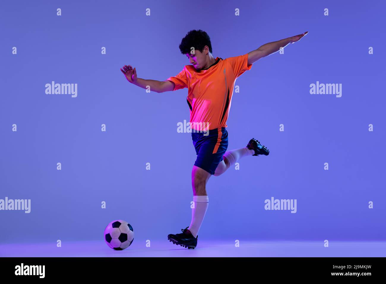 Studio shot of male professional football, soccer player practicing ...