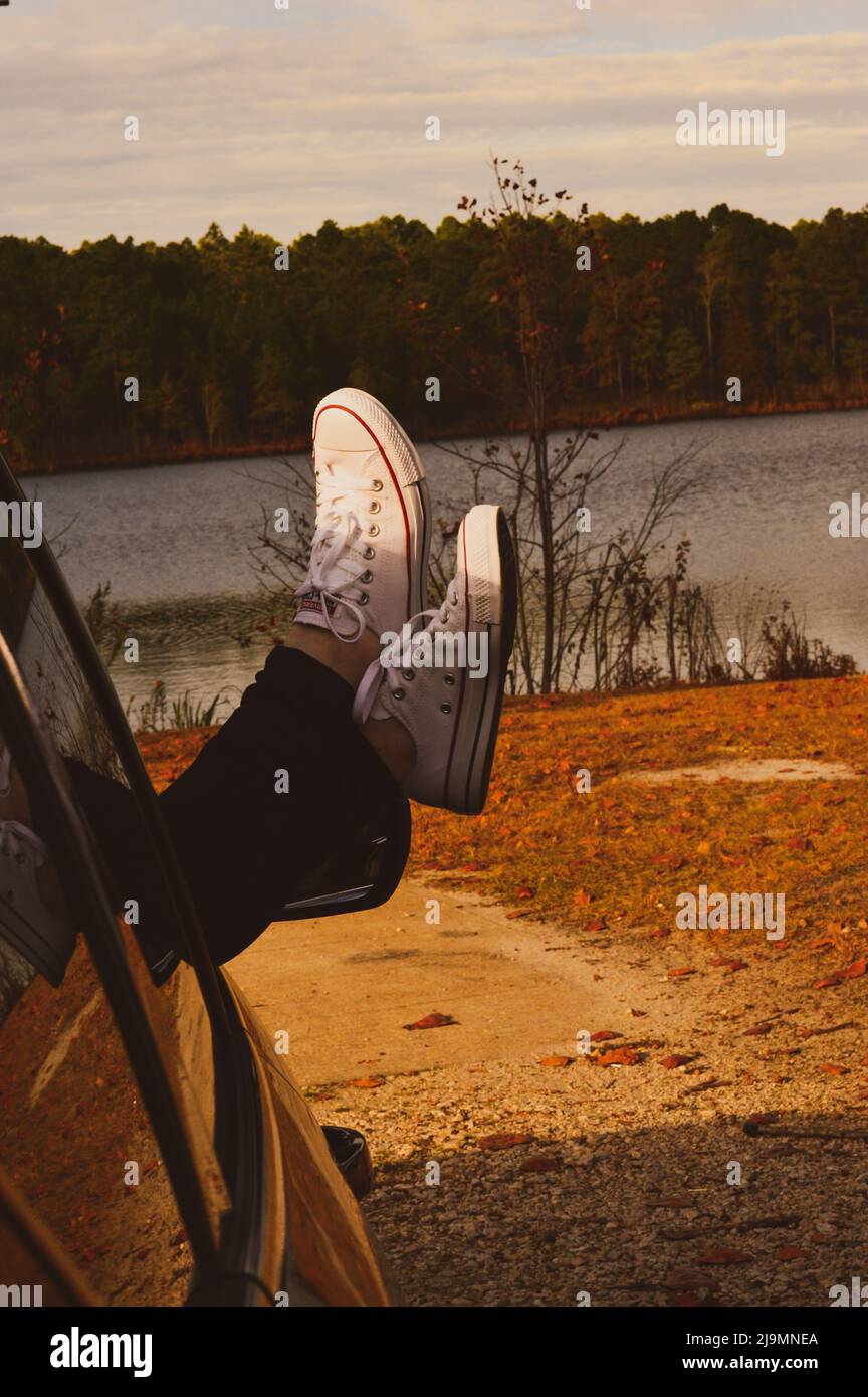 Traveling young woman relaxing by lake with feet out window at sunset ...
