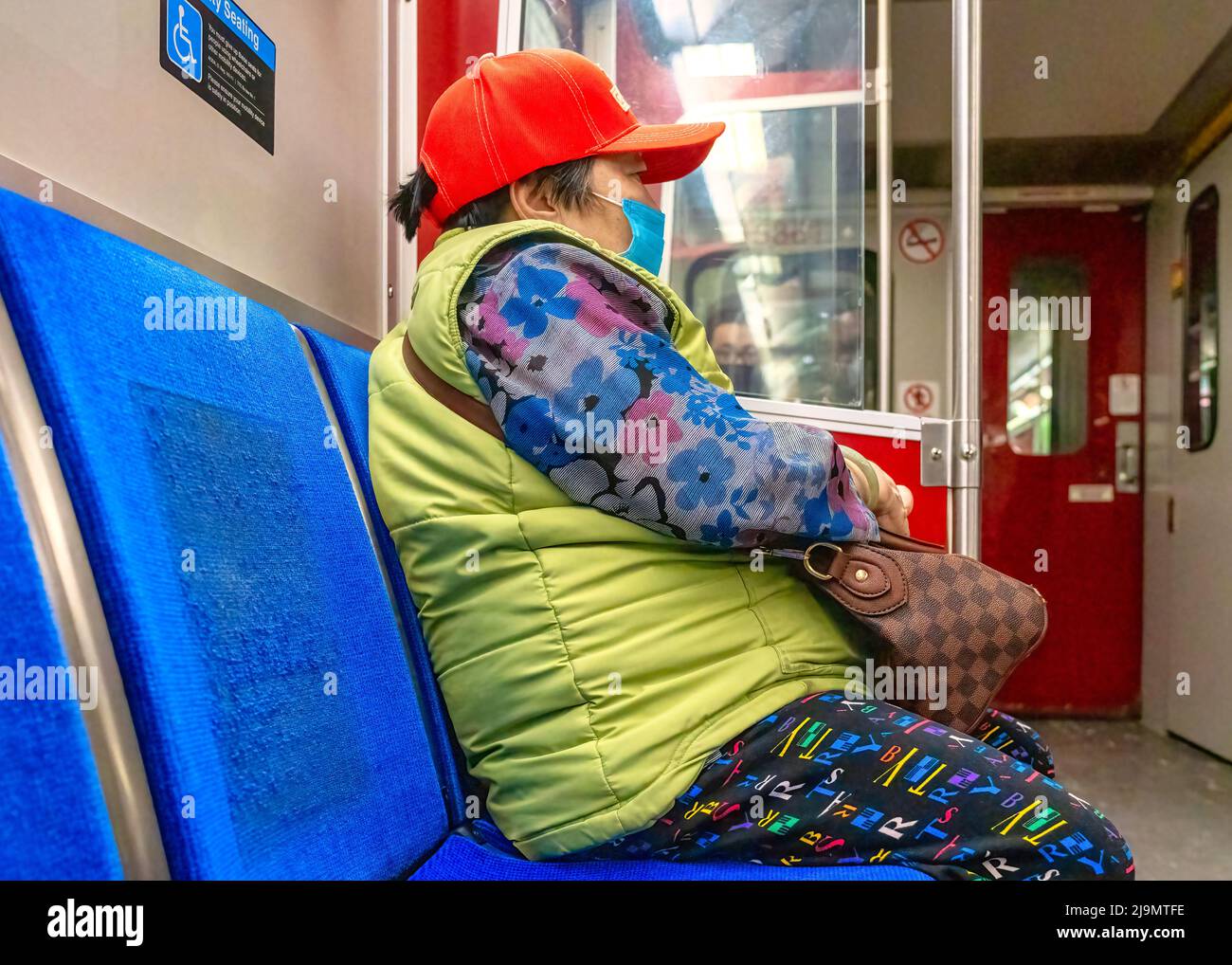 A woman rides in a TTC subway train wearing colorful clothes and a ...