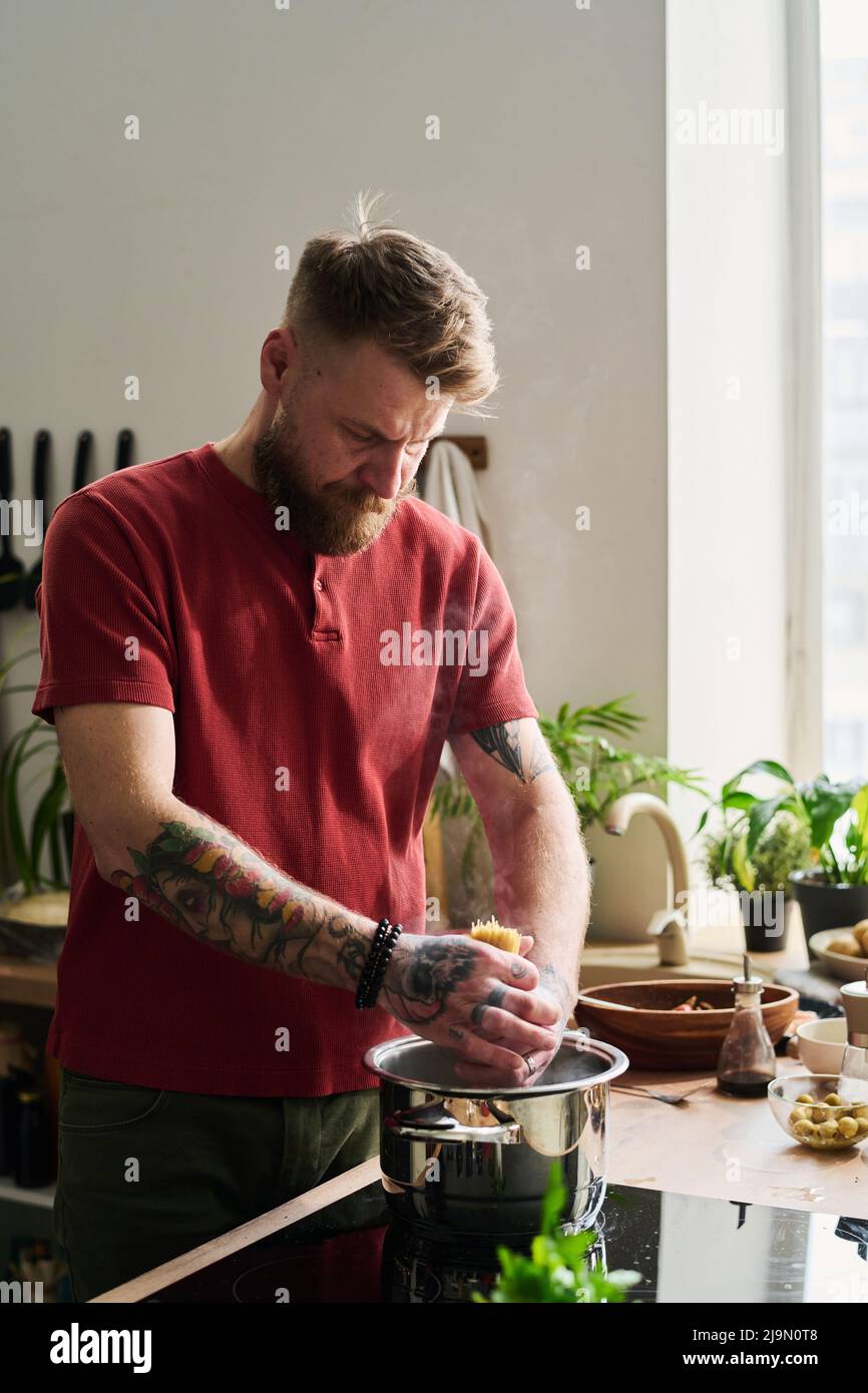 Modern Caucasian chef standing in loft kitchen at home putting ...