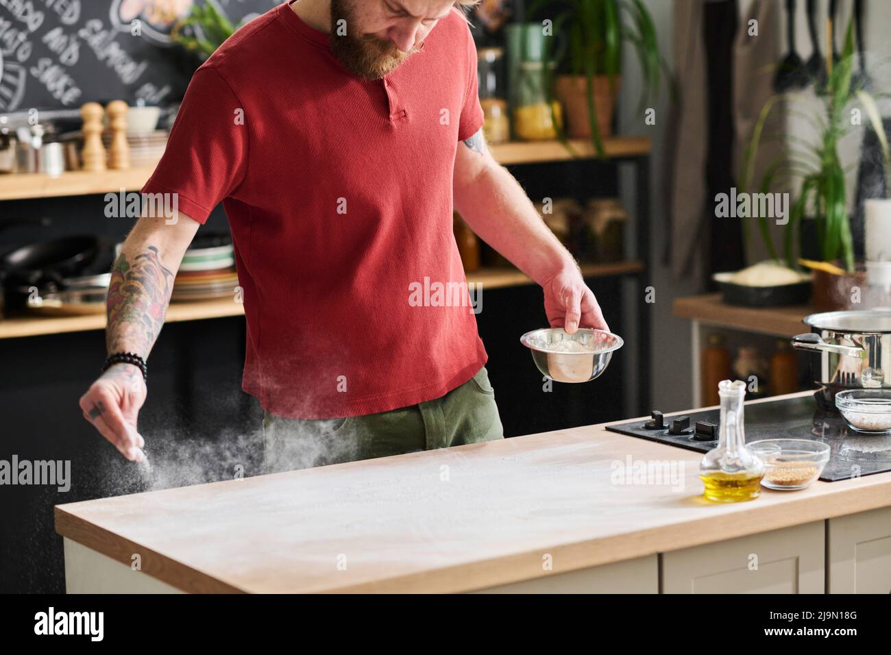 Modern professional chef in casual clothes dusting kitchen table with ...