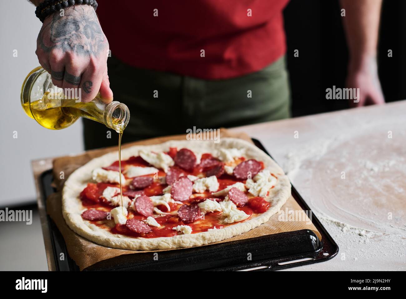 Unrecognizable male food blogger pouring olive oil over homemade pizza ...