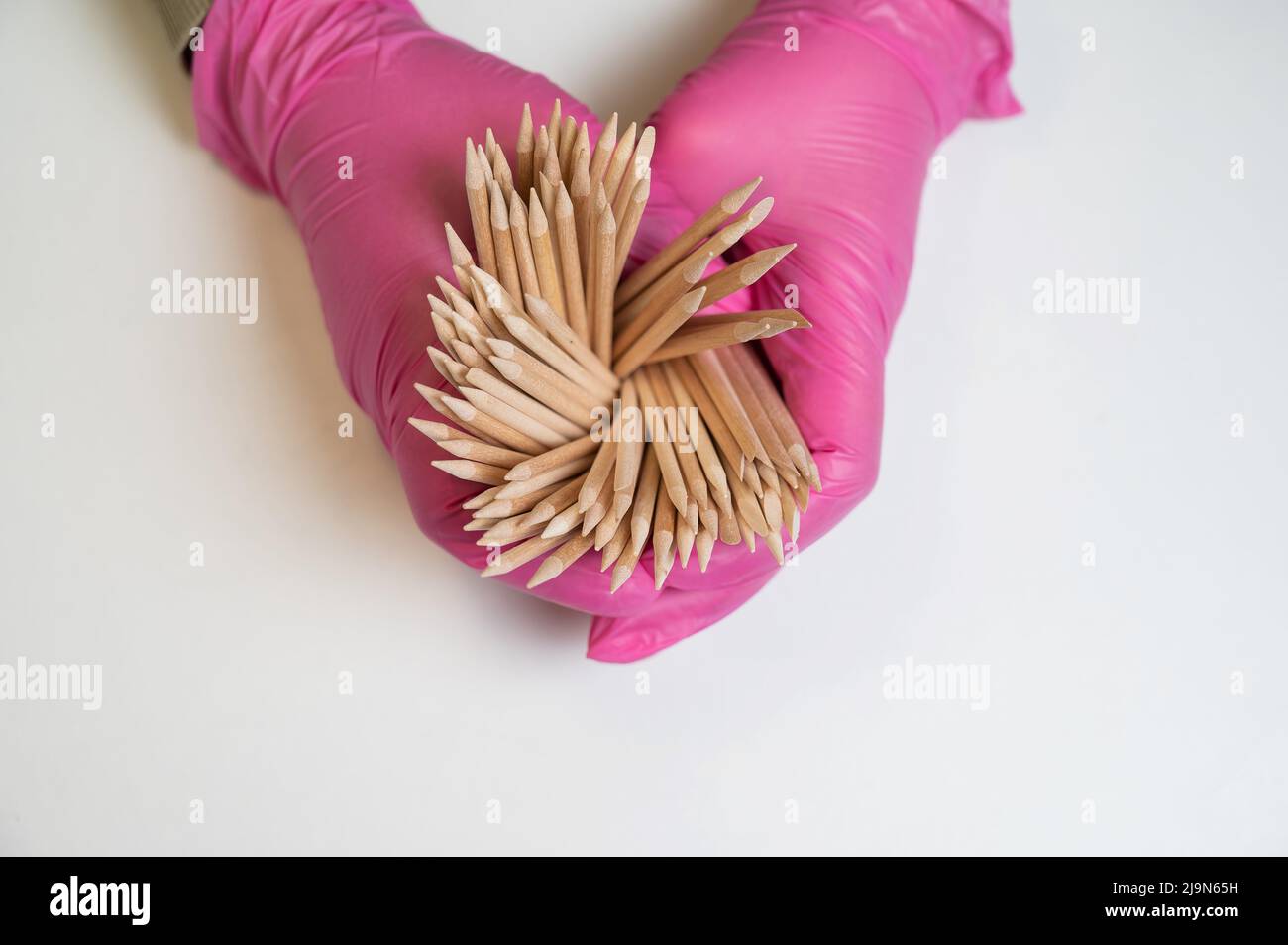 Master in pink gloves holds orange sticks for manicure Stock Photo - Alamy