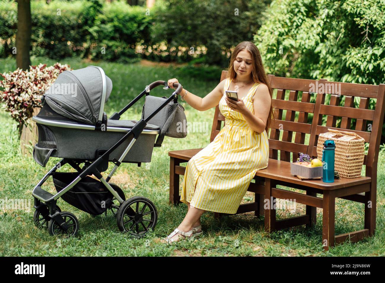 Apps for mom. Young mother with newborn baby in stroller using mobile ...