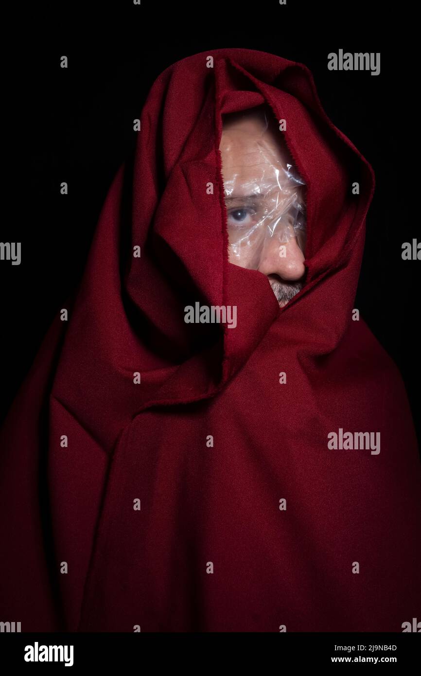 Man covered in red cloth with plastic on his face against black ...