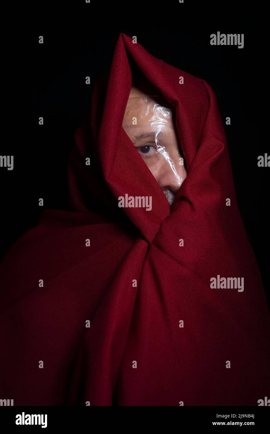 Man covered in red cloth with plastic on his face against black ...