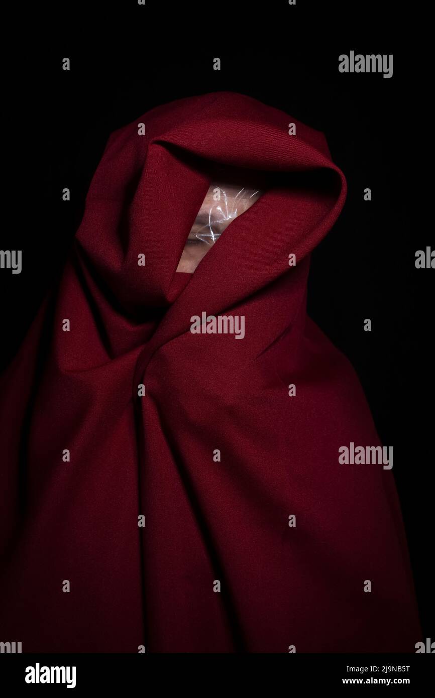 Man covered in red cloth with plastic on his face against black ...