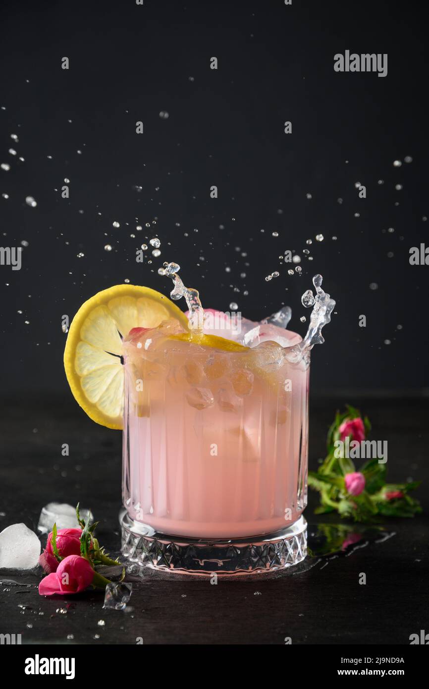 Pink gin cocktail garnish lemon and rose flowers on black background ...