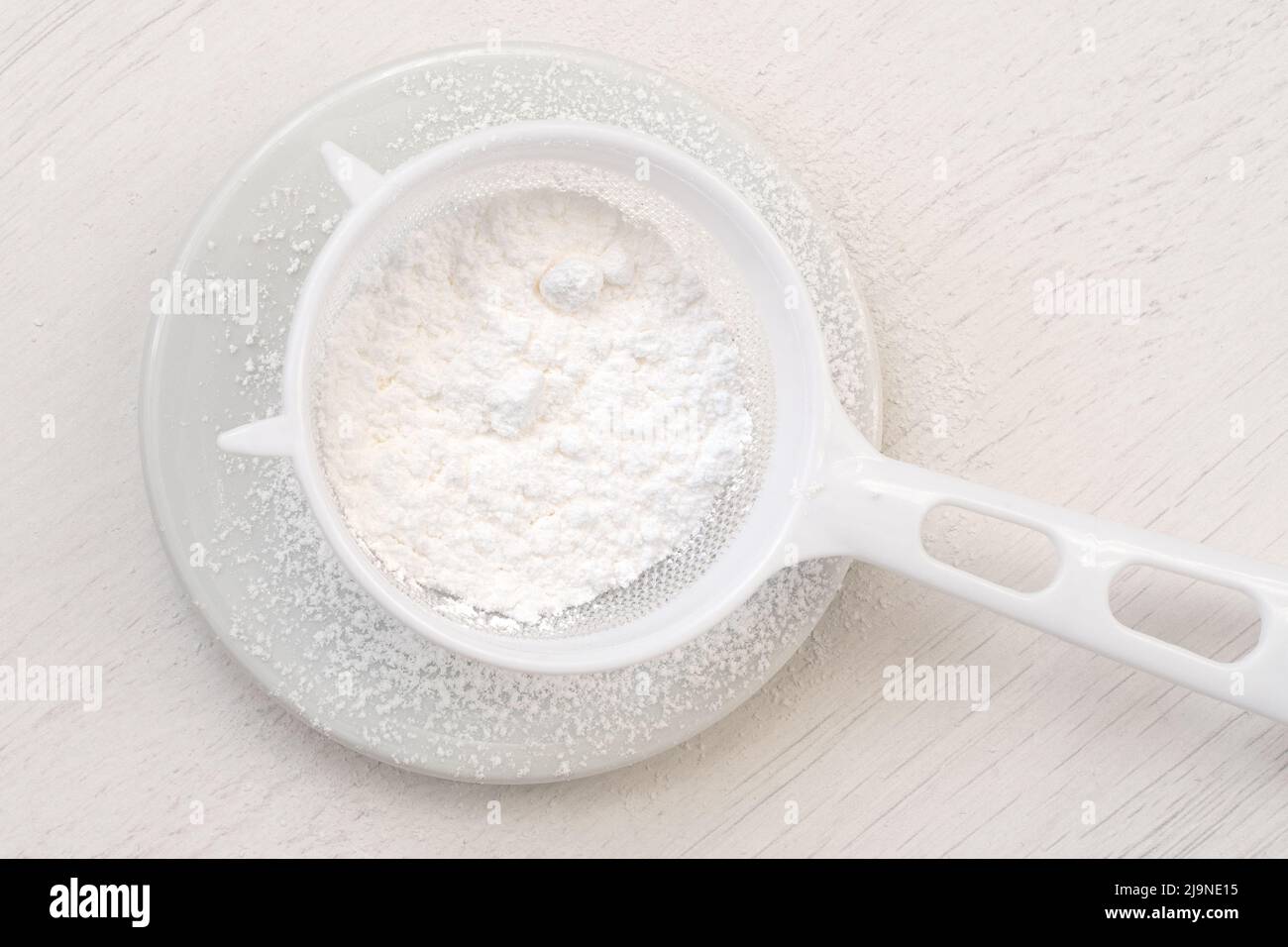 Icing sugar in a plastic sieve on top of white ceramic plate on white ...