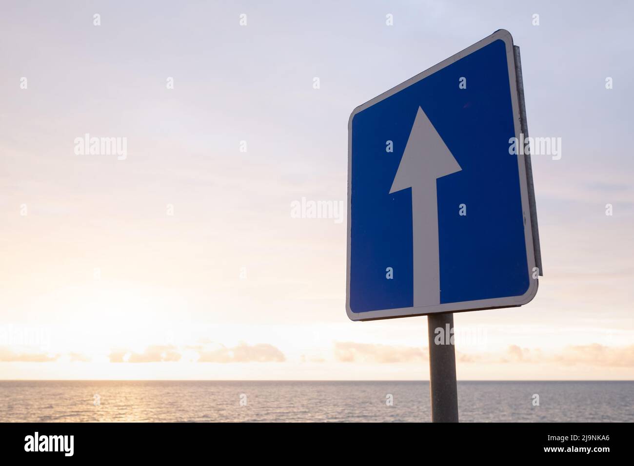Square road sign with white arrow on blue sky background. It indicates ...