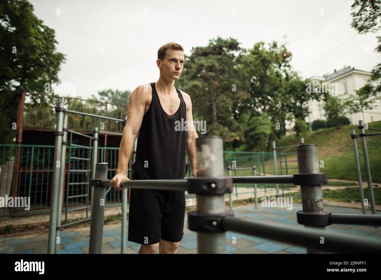 Fit man doing triceps dips on parallel bars at park exercising outdoors ...