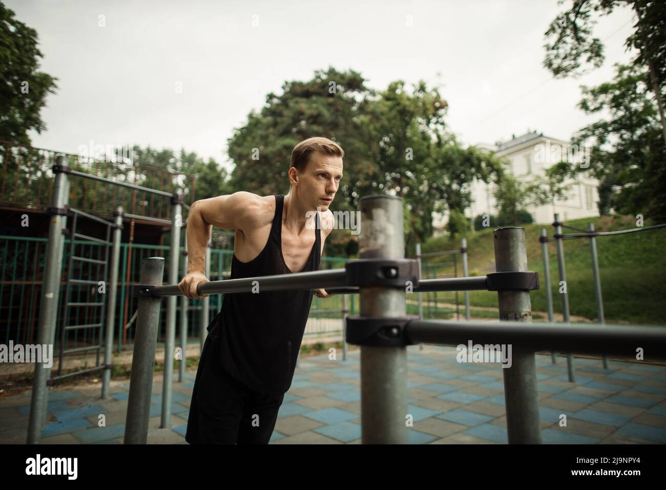 Fit man doing triceps dips on parallel bars at park exercising outdoors ...