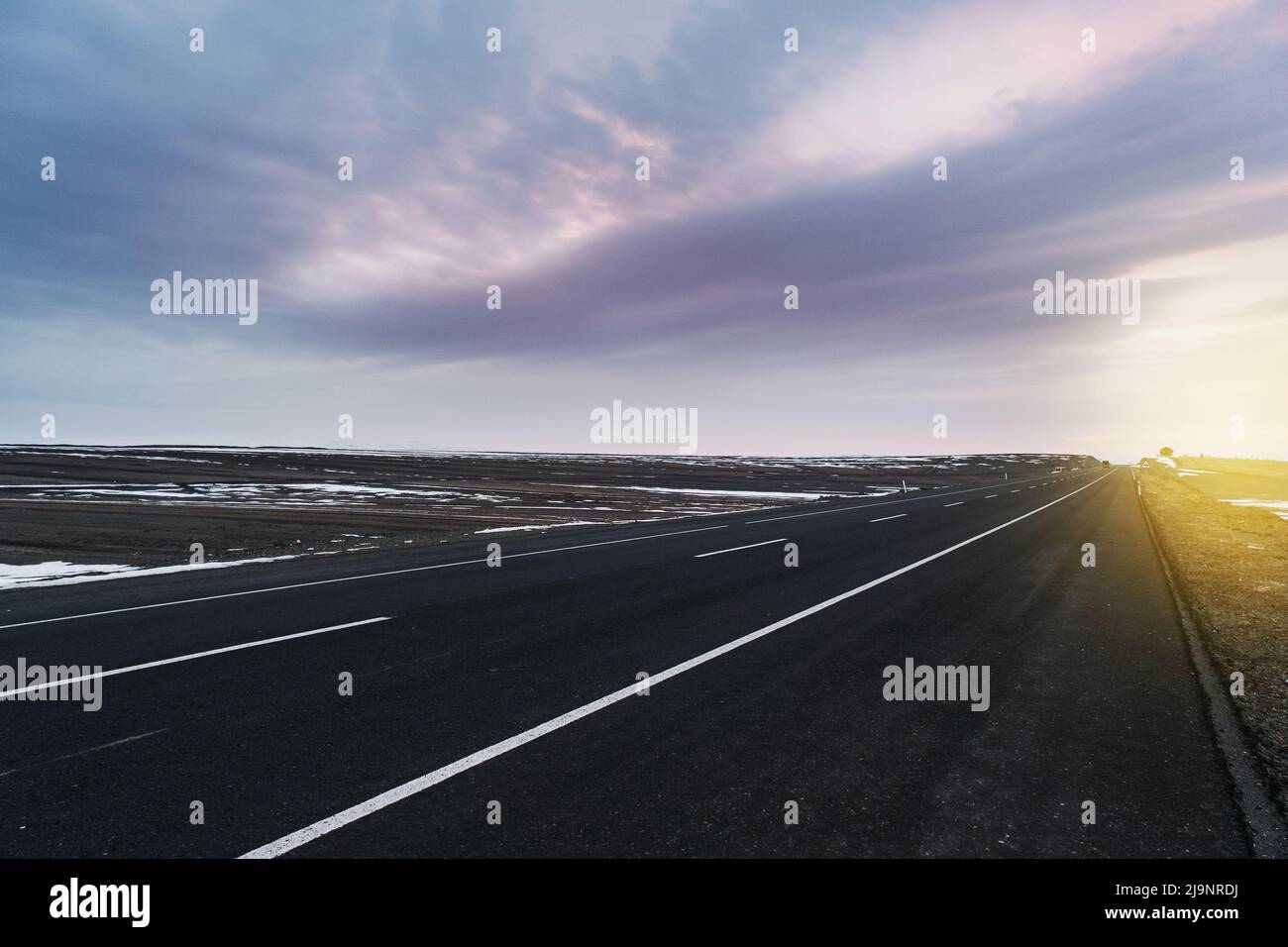 Diagonal view of an emtpy asphalt road with lanes and snow in winter ...