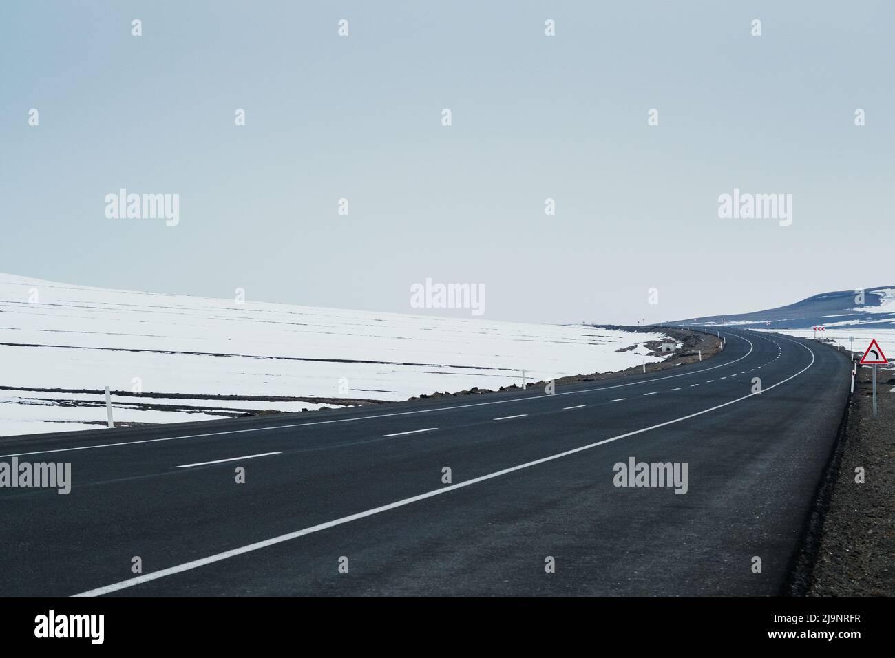 Diagonal view of an emtpy asphalt and bending road with lanes and snow ...
