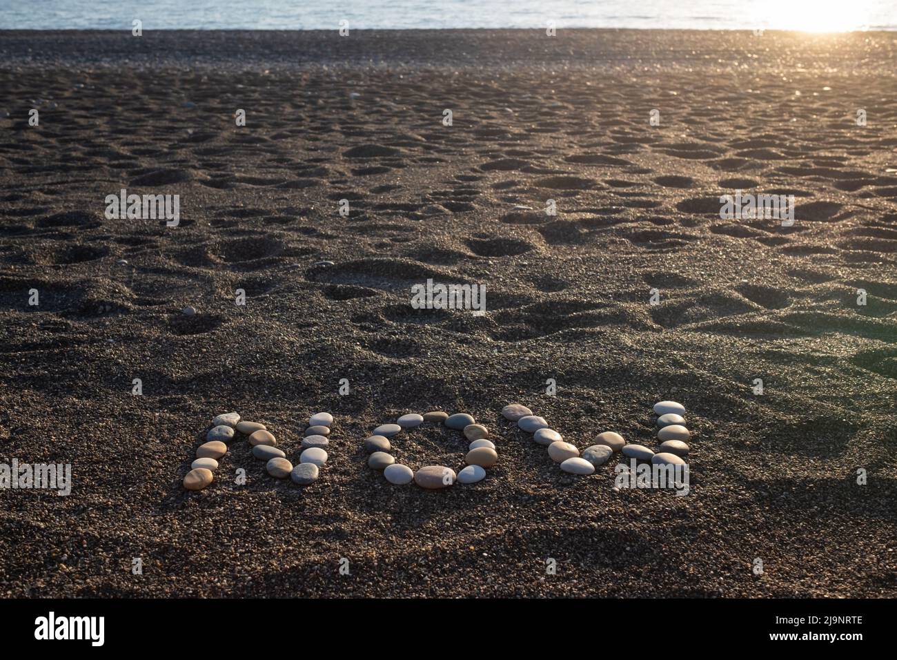 Word now made form stones on sandy beach Stock Photo - Alamy