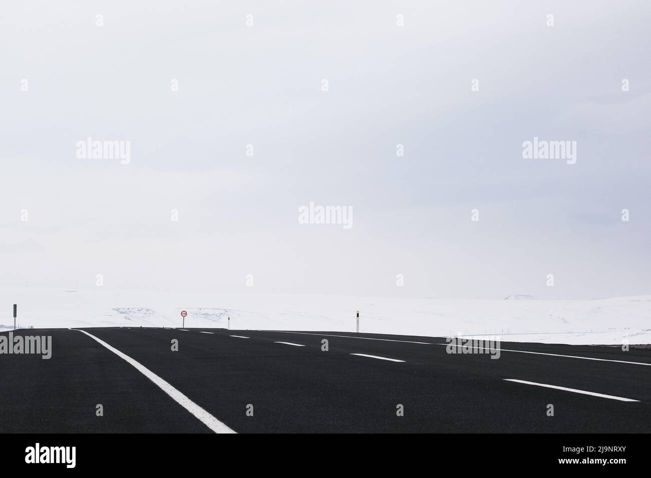 Diagonal view of an emtpy asphalt and bending road with lanes and snow ...