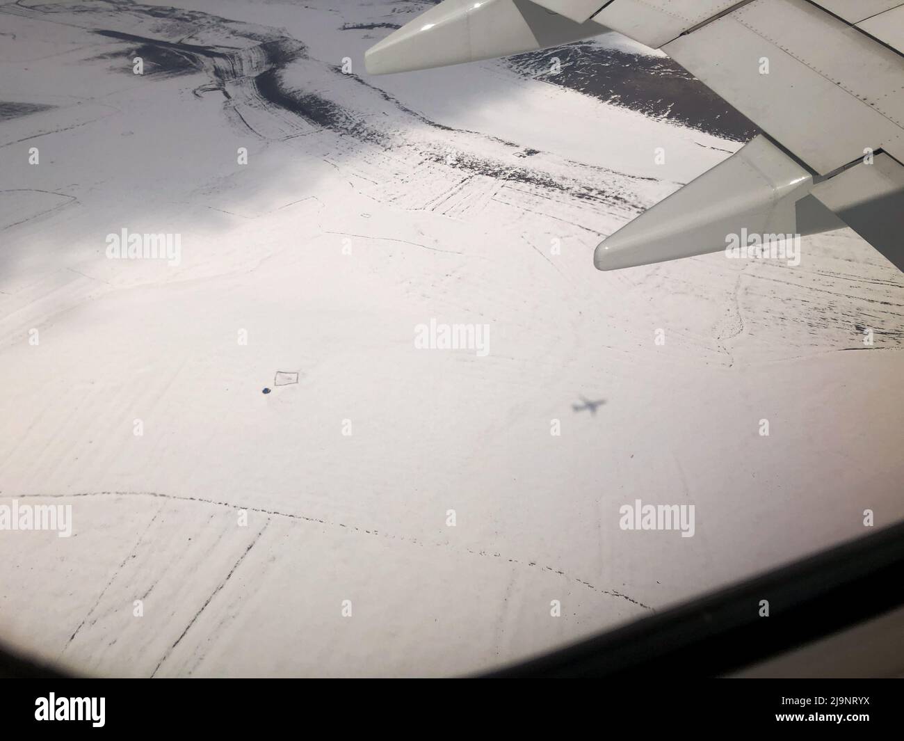 Snowy landscape view from a commercial airplane's window and shadow of ...