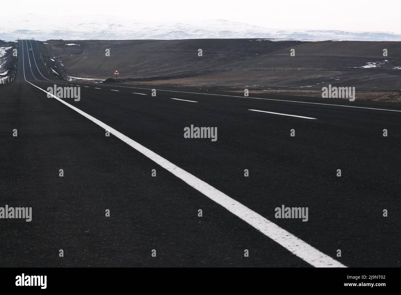 Diagonal view of an emtpy asphalt and bending road with lanes and snow ...