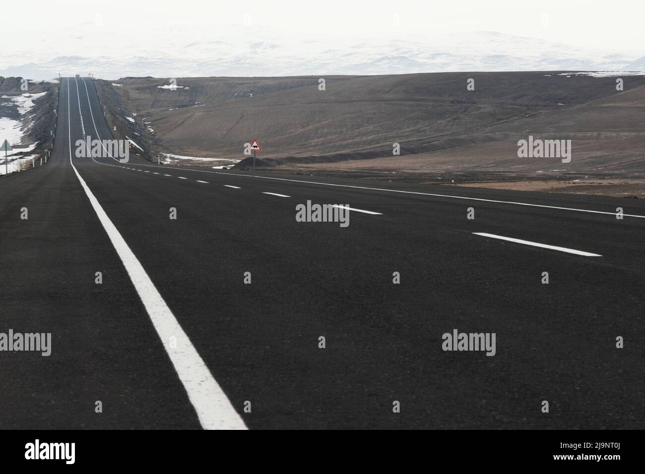 Diagonal view of an emtpy asphalt and bending road with lanes and snow ...