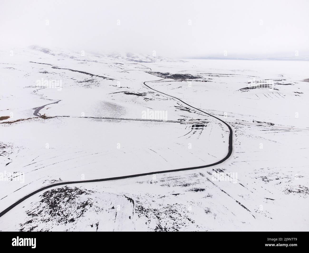 Aerial top view of a S shaped road with one lane and snow in winter ...