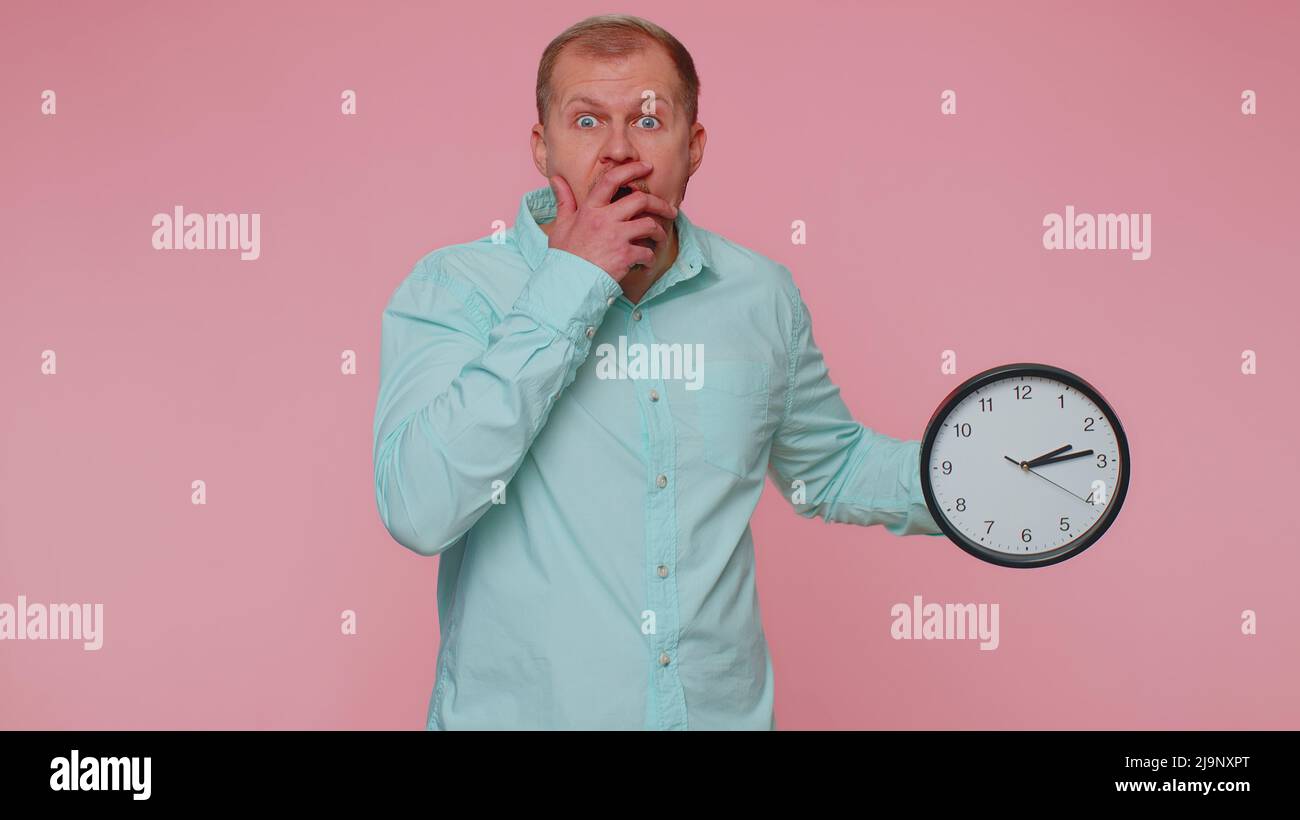 Confused man with anxiety checking time on clock, running late to work ...