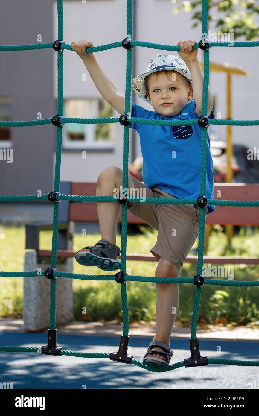 Portrait of cute smiling boy climbing up the rope net he look at camera ...
