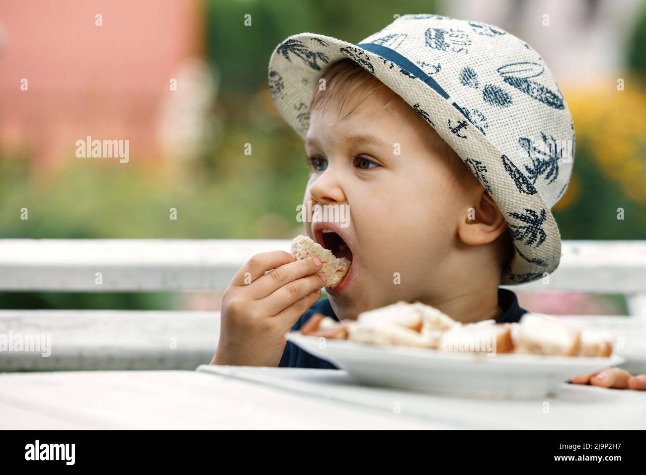 Close-up portrait of cute little child eating bread in green garden ...
