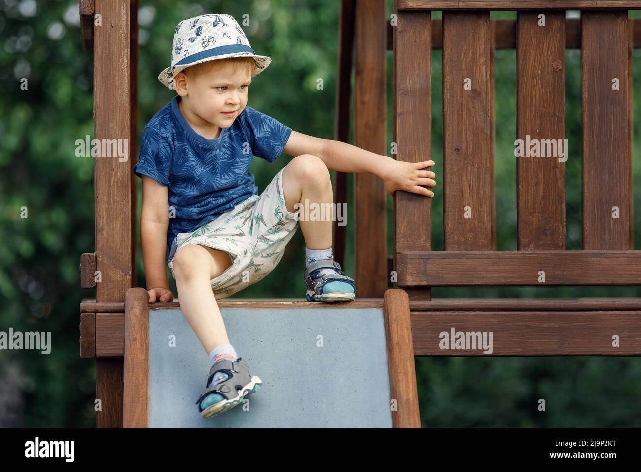 A child climbs up on the wooden playground and prepares to slide on a ...