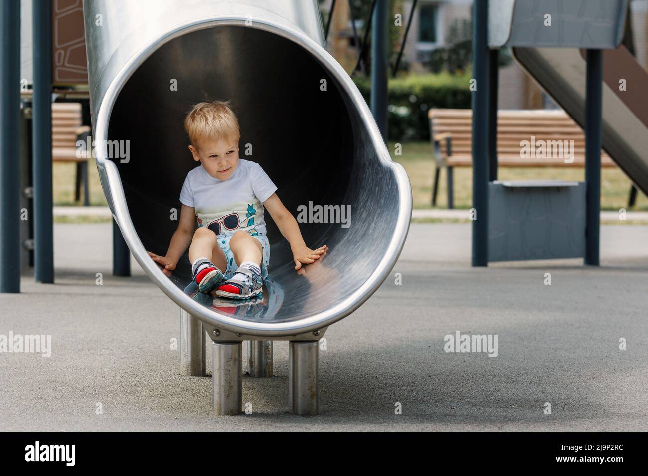 A boy slides down a metal enclosed circular tunnel slide. A child ...