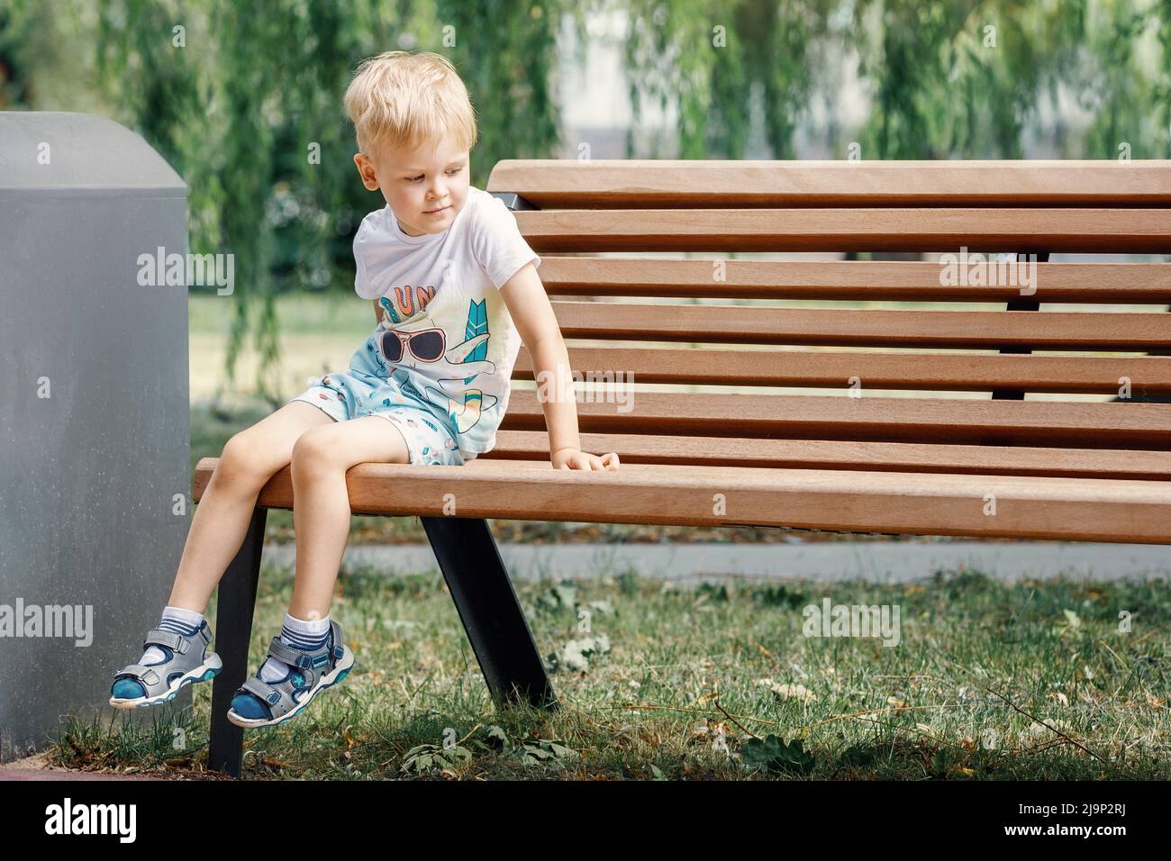 Small child plays in park, climbs onto bench. Kid is sitting on a park ...