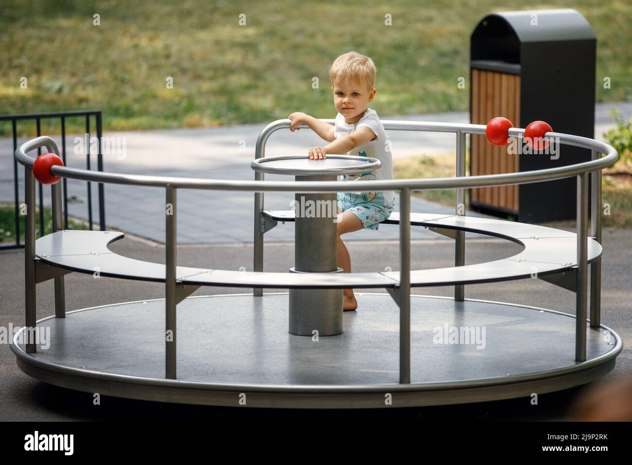 A little boy sits in a metal carousel for children in summer in the ...
