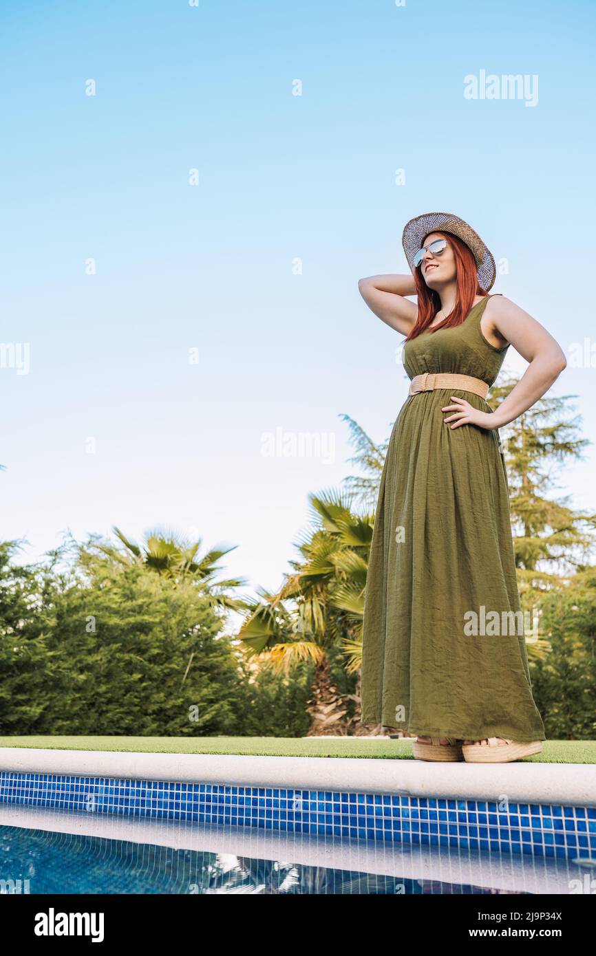adventurous young woman, standing sunbathing in front of the swimming pool of her holiday hotel ...