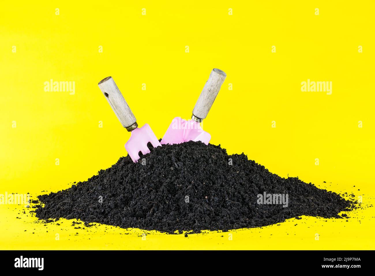 A pile of soil, earth with a pink trowel and fork pushed into it ...