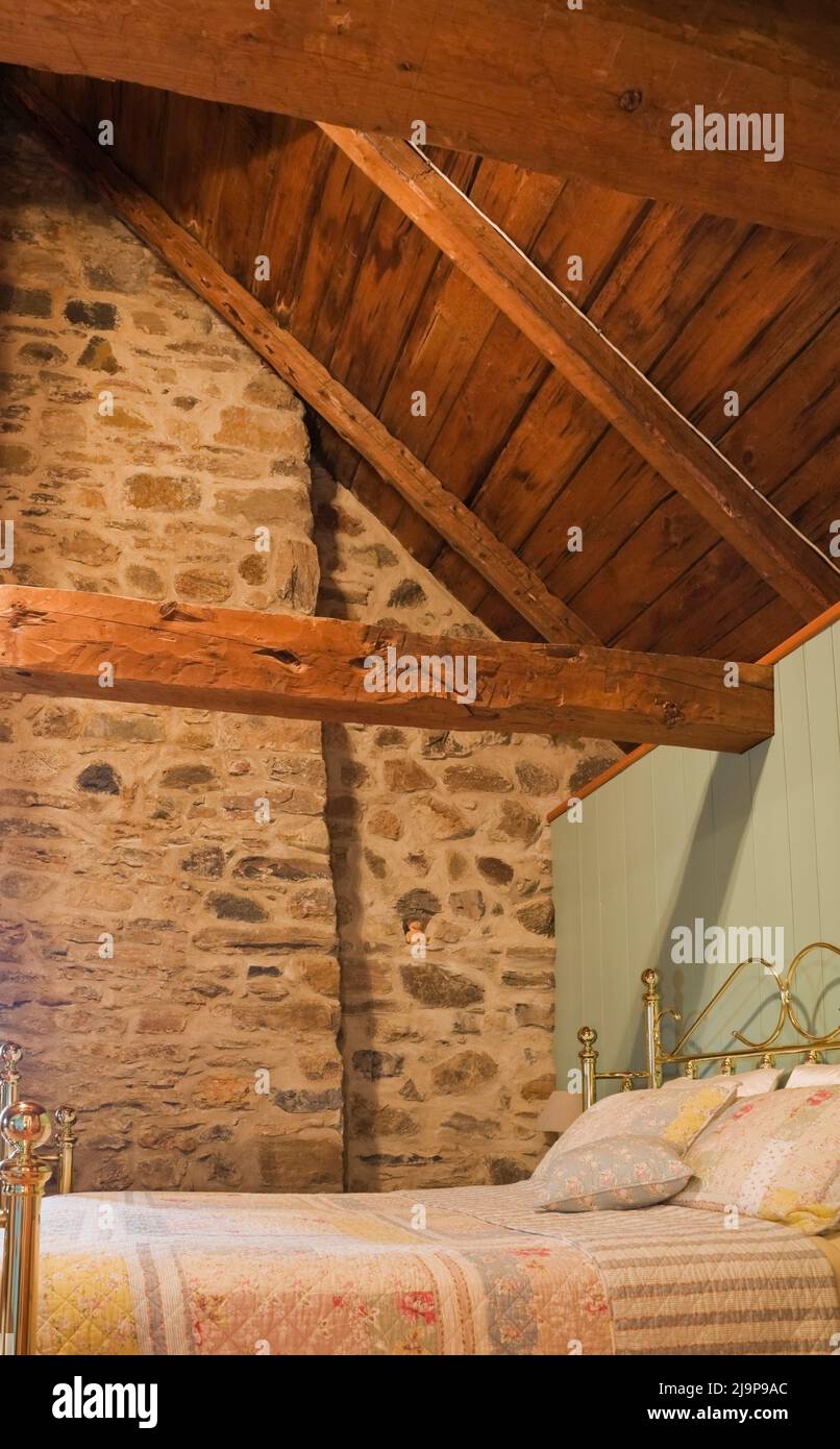 Brass bed and exposed wooden beams, rafters and roof boards and attic ...