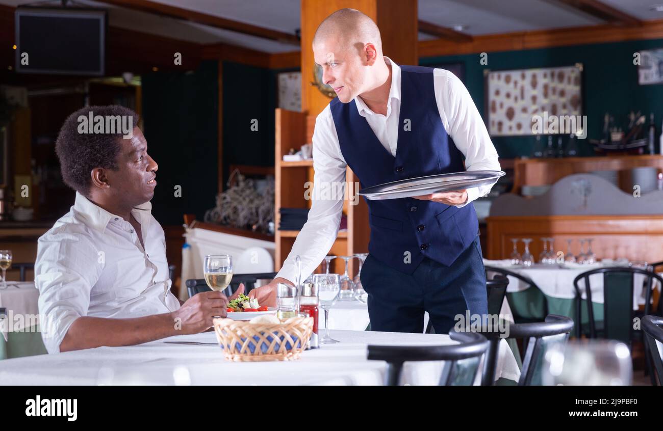 Friendly waiter serving cheerful African American in restaurant Stock ...