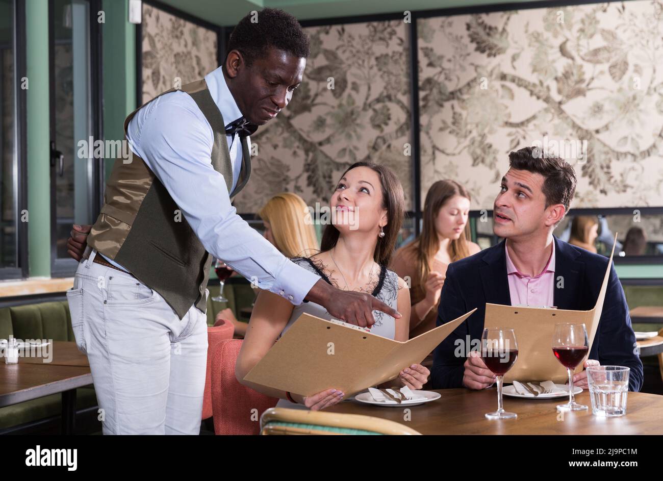 African American waiter helping couple with menu Stock Photo - Alamy