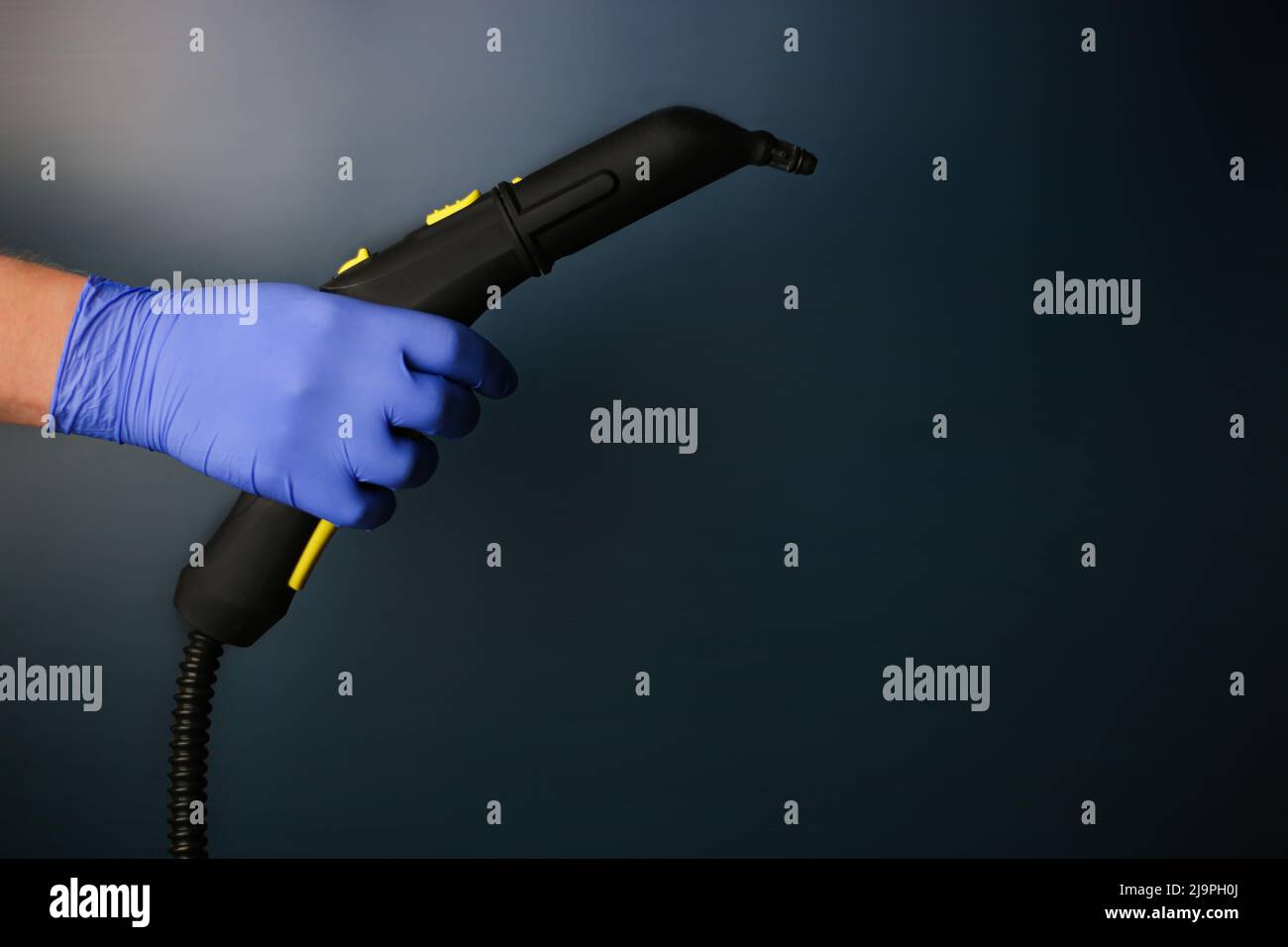 Steam cleaner in hand with hot steam on an isolated dark background ...