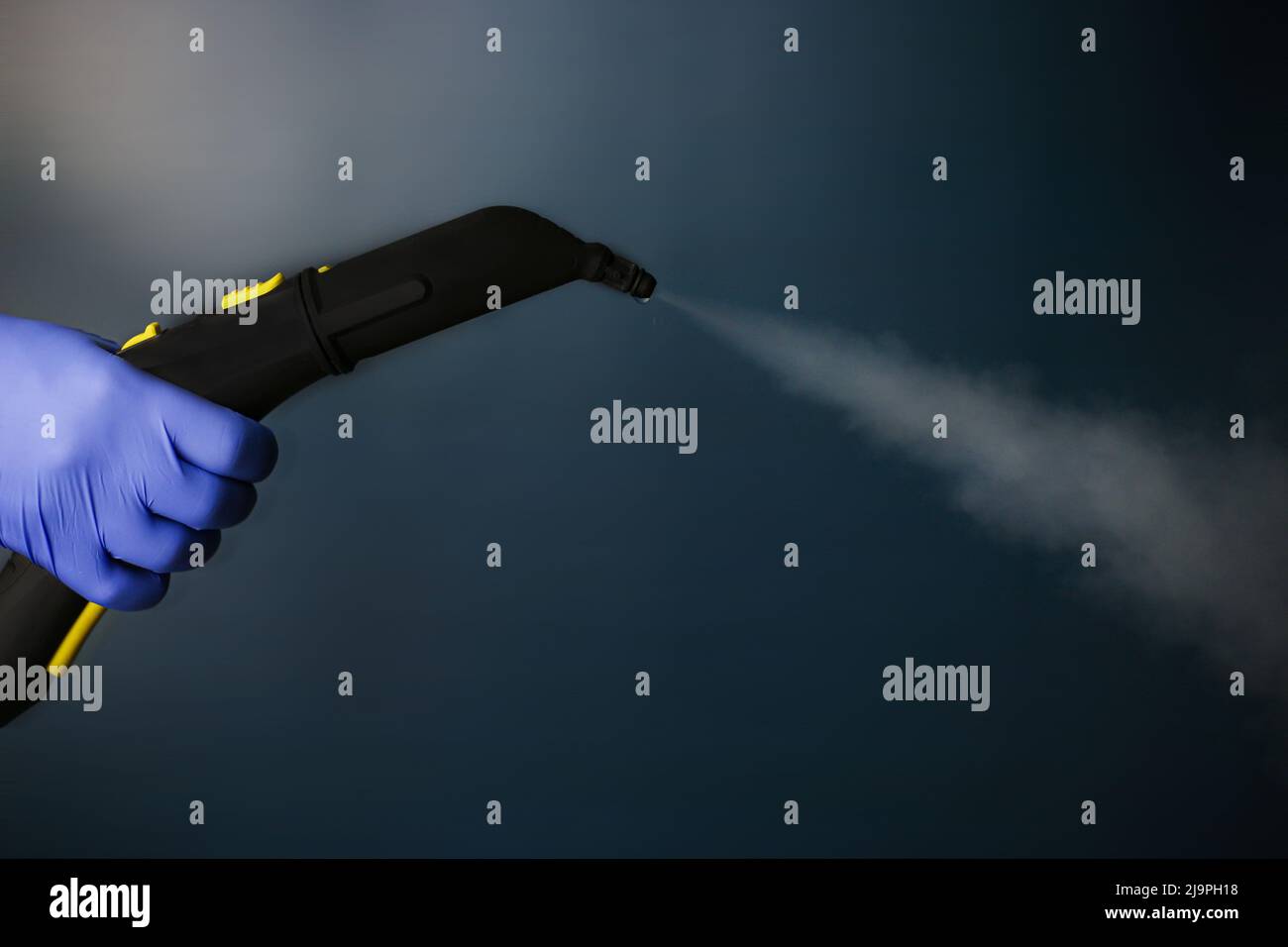 Steam cleaner in hand with hot steam on an isolated dark background ...