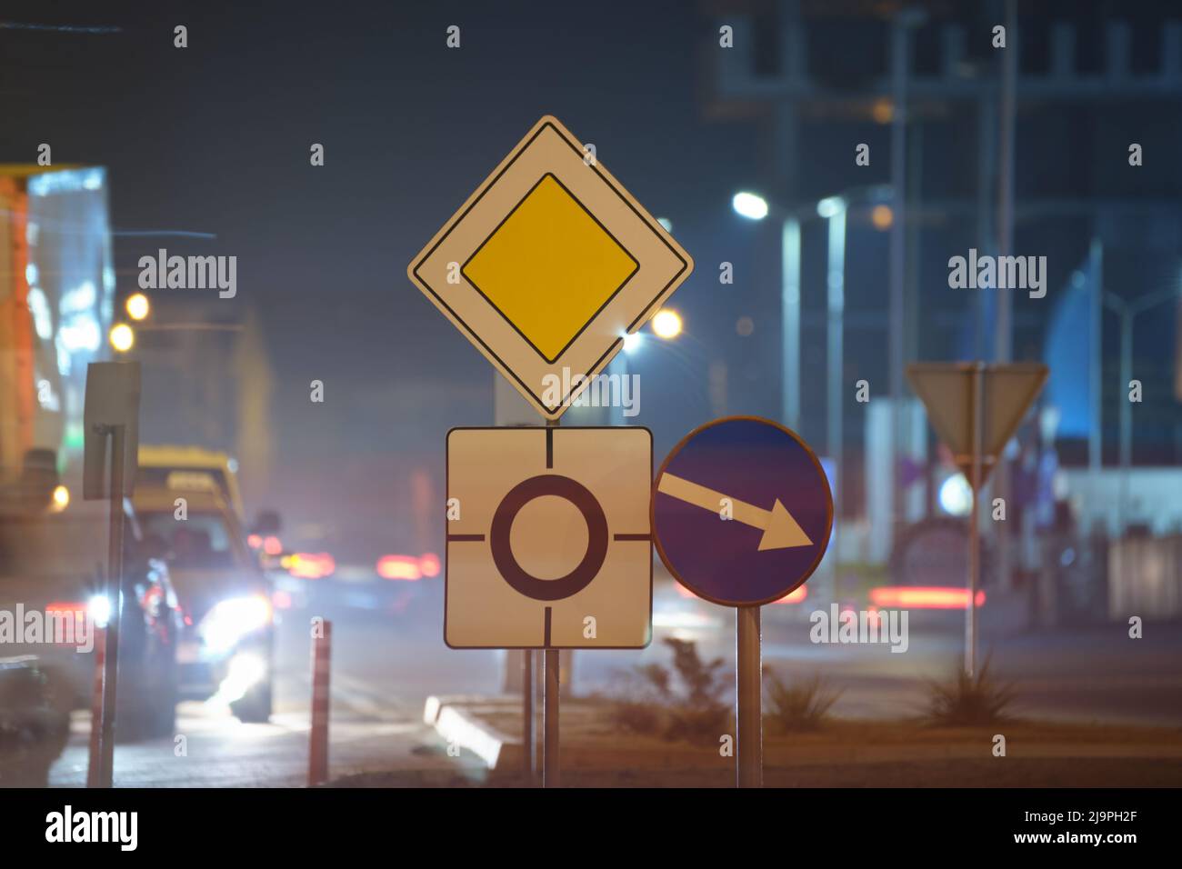 Roundabout road signs with blurred cars on city street traffic at night ...