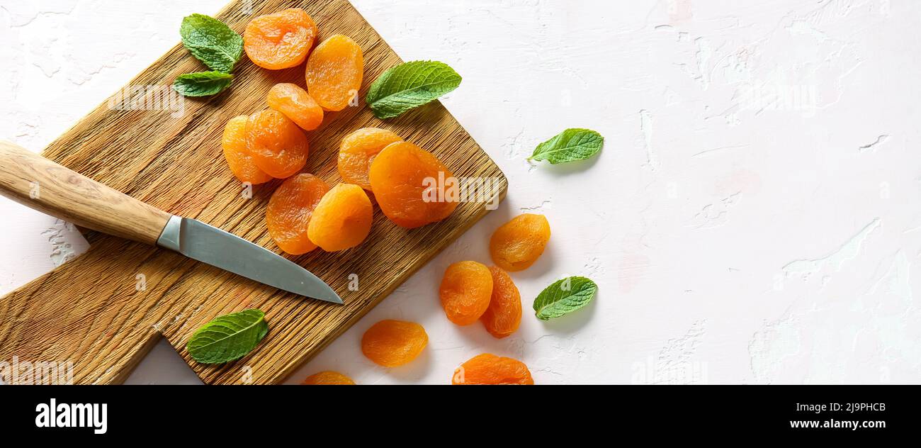 Wooden board with dry apricots and knife on light background with space ...