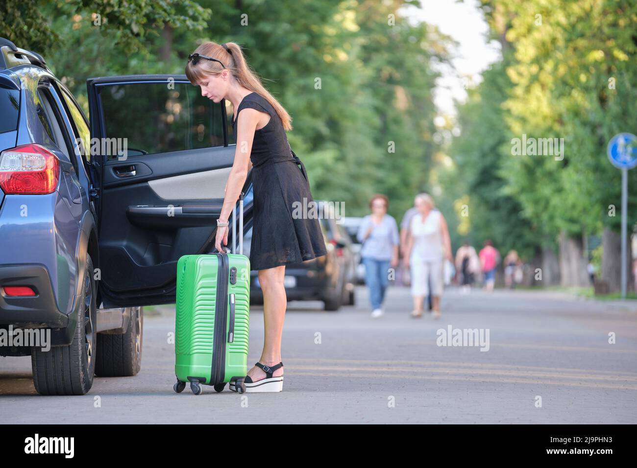 Young female driver loading luggage suitcase bag inside her car ...