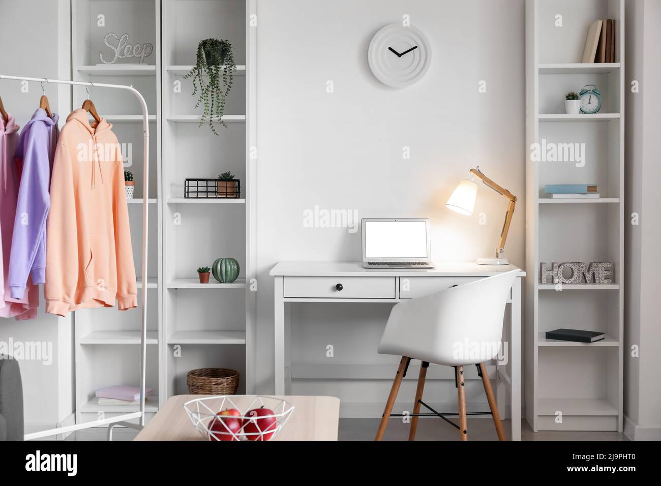 Interior of light room with modern workplace, rack and hoodies Stock ...