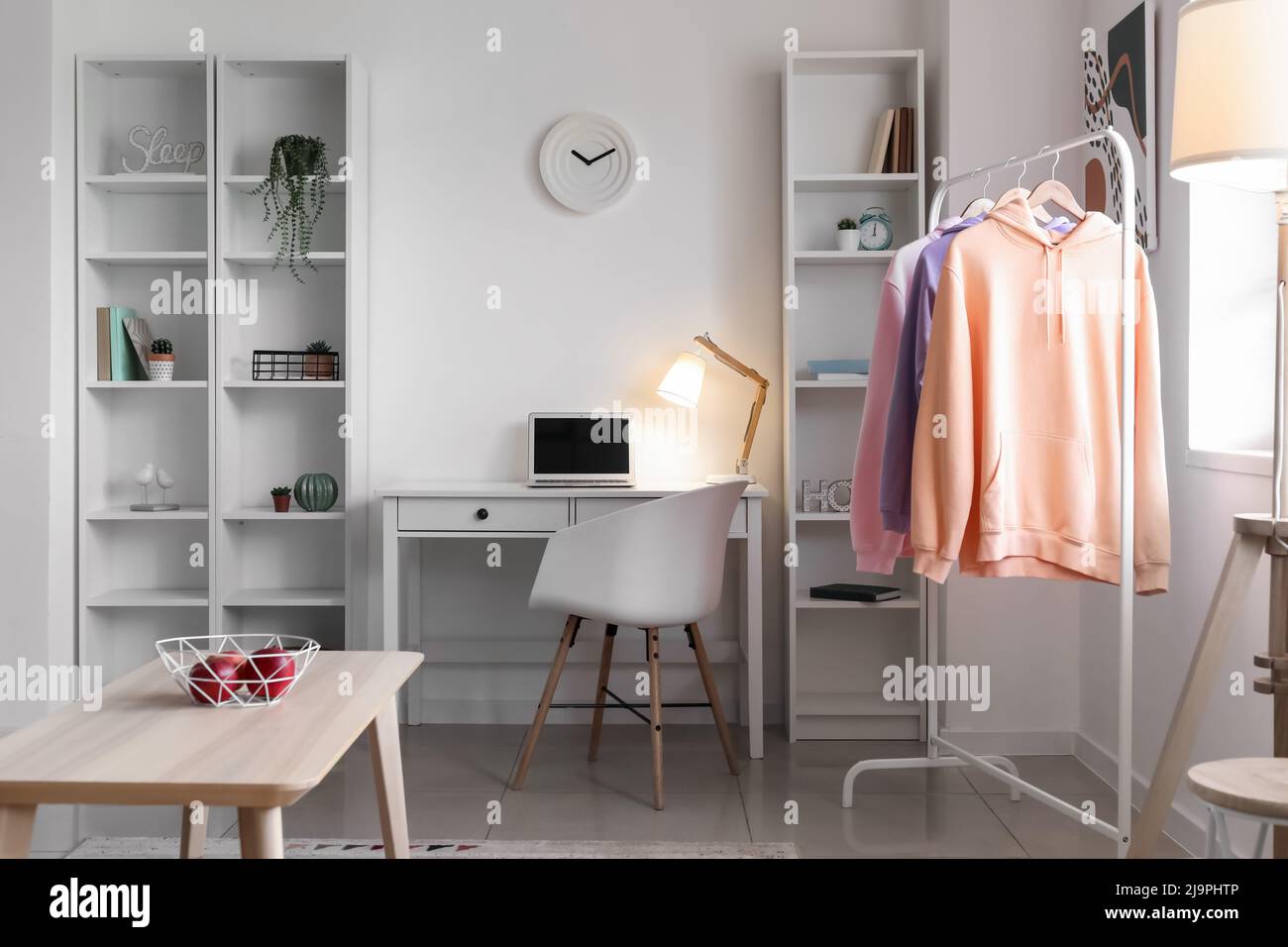 Interior of light room with modern workplace, rack and hoodies Stock ...