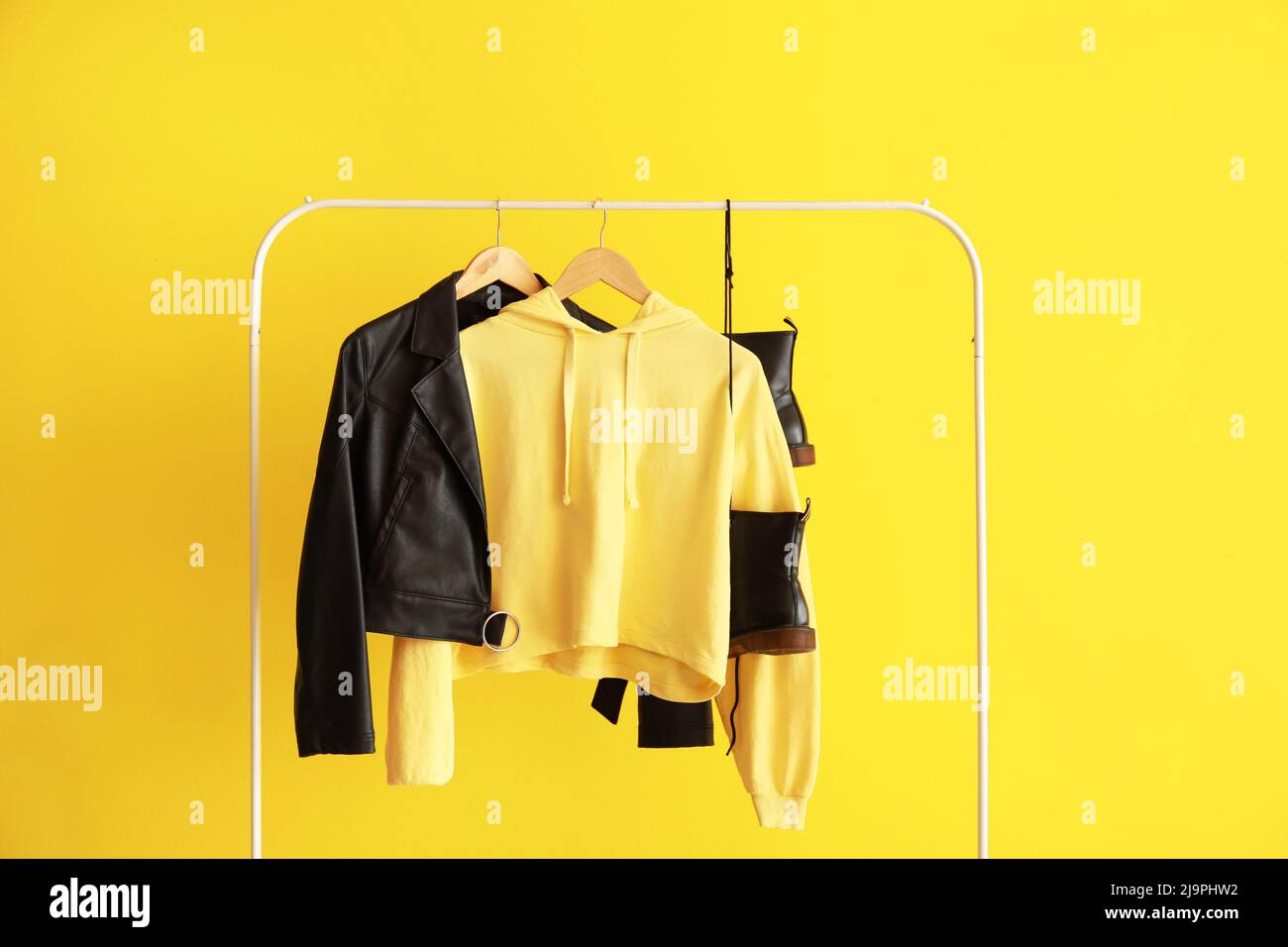 Rack with hoodie, jacket and boots near yellow wall Stock Photo - Alamy
