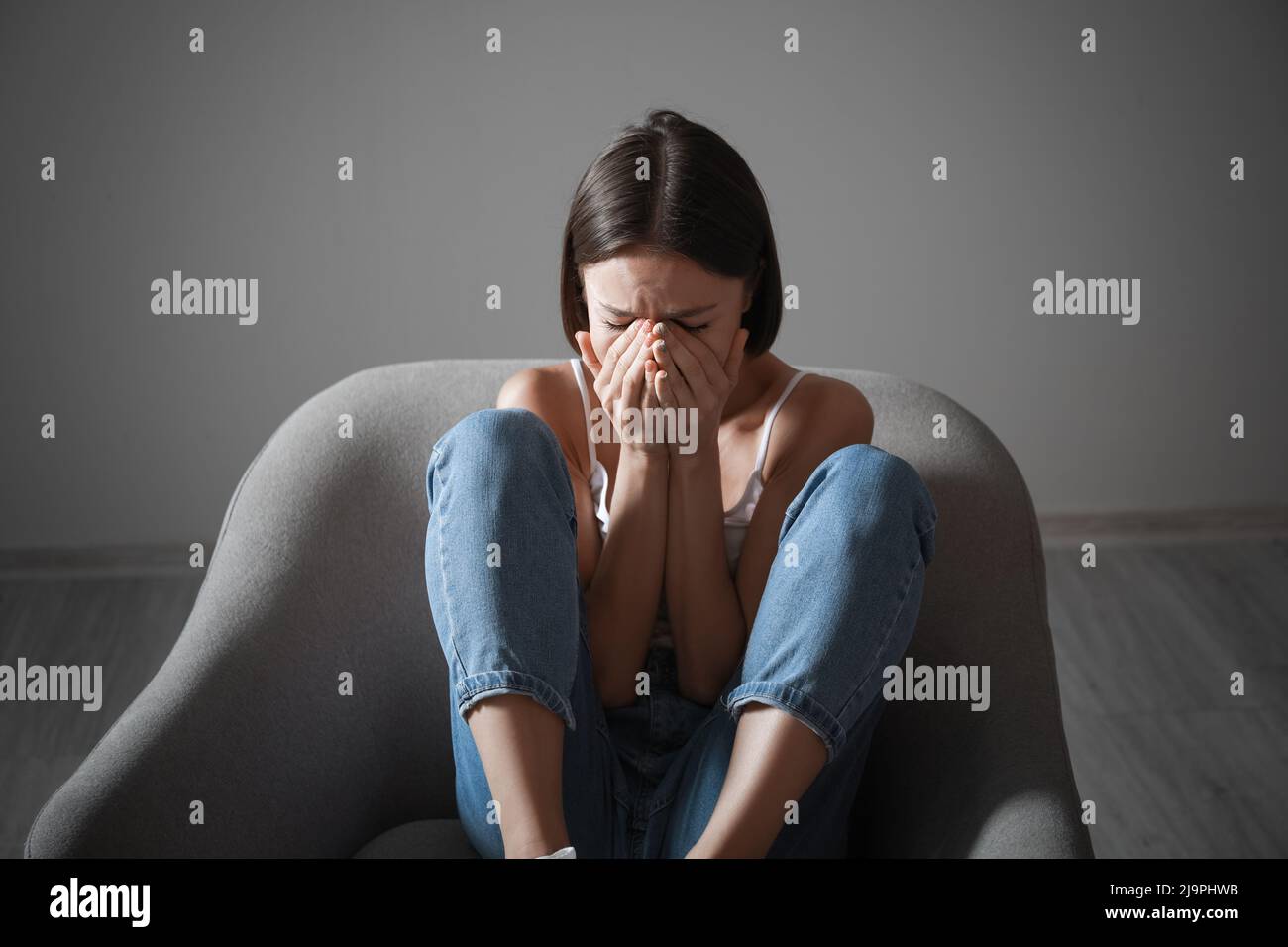 Crying young woman sitting in armchair at home. Violence concept Stock ...